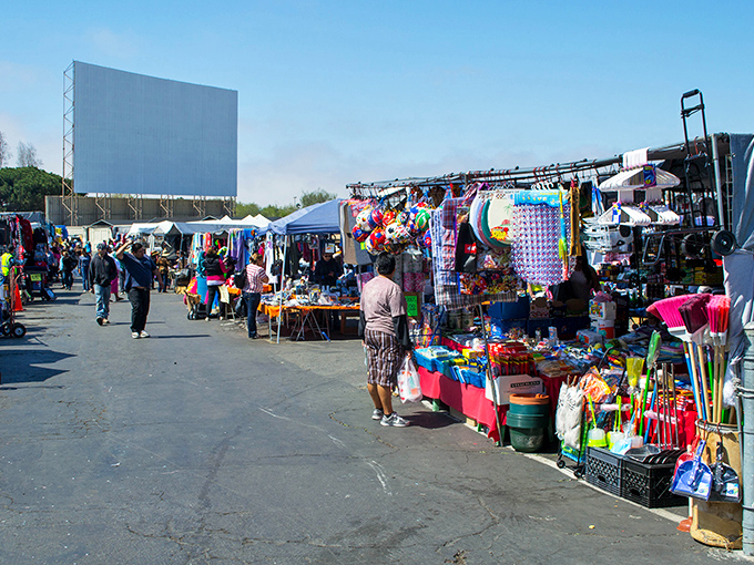 The iconic drive-in movie screen looms over a colorful sea of vendors, where morning bargain hunters navigate aisles of potential treasures.