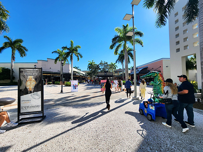 Palm trees standing tall like well-dressed doormen, welcoming shoppers to a paradise where credit cards get their own vacation. The cobblestone walkway practically whispers "fancy bargains ahead."