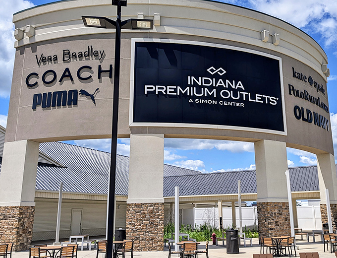 The retail promised land beckons with its siren song of discounts. Coach, Vera Bradley, and Puma logos hint at the treasures waiting inside.