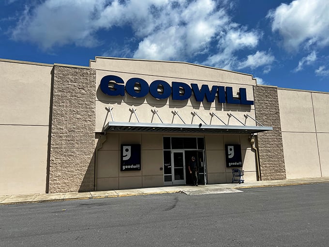 The iconic blue Goodwill sign beckons like a lighthouse for bargain hunters navigating the sea of retail.