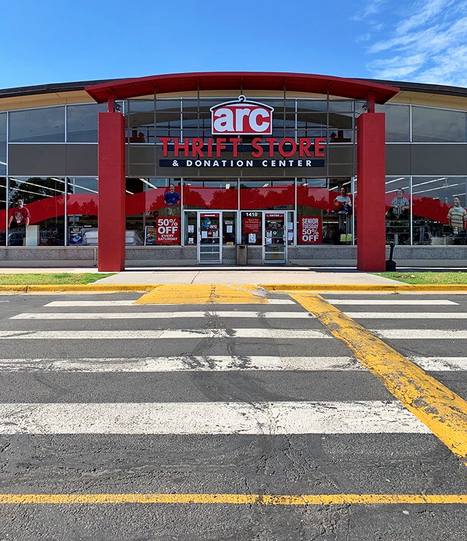 The red-trimmed facade of arc Thrift Store stands like a treasure chest waiting to be opened, promising adventures in secondhand splendor.