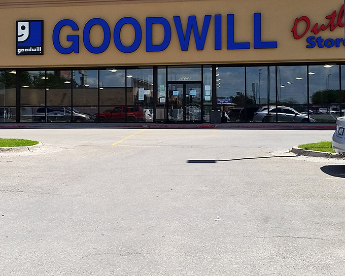 The blue Goodwill Outlet sign beckons like a siren call to treasure hunters. This unassuming exterior houses an indoor archaeological dig waiting to happen.