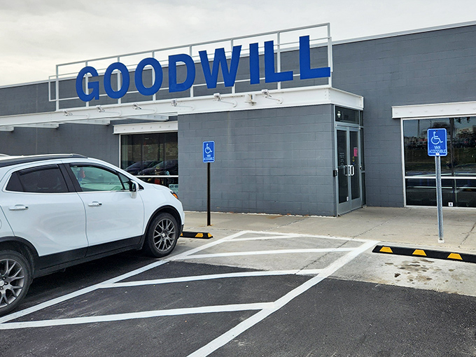 The blue Goodwill sign beckons like a lighthouse for bargain hunters, promising treasures within those unassuming gray walls.