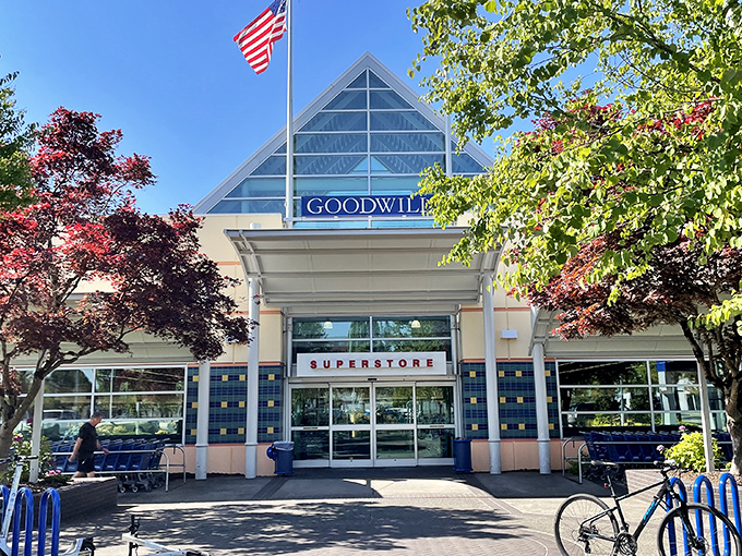 The distinctive triangular glass entrance of Portland's Goodwill Superstore stands like a temple to thrift, complete with American flag proudly waving above treasure-hunters paradise.