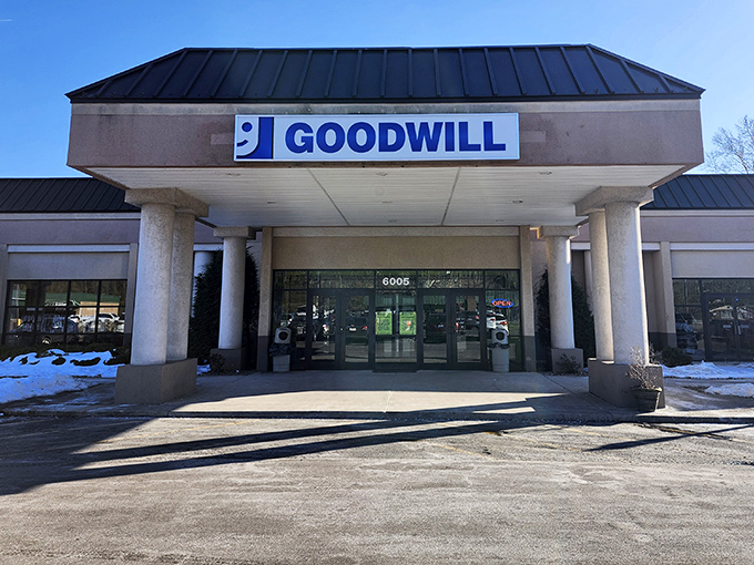 The blue Goodwill sign beckons like a lighthouse for bargain hunters. Behind these doors, retail adventures await that no mall can match.