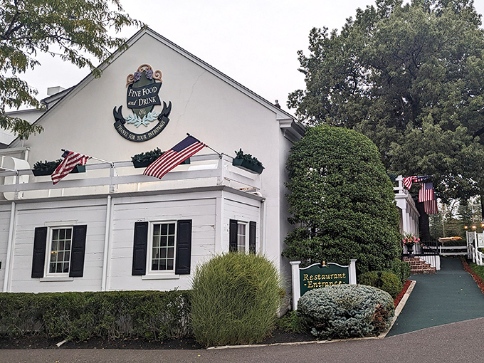 Colonial charm meets culinary excellence at the William Penn Inn's pristine white exterior, where American flags flutter like dinner invitations in the Pennsylvania breeze.