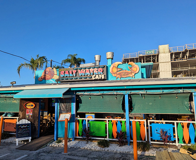 The vibrant turquoise exterior of Frenchy's Saltwater Cafe welcomes beach-goers with its colorful surfboard railings and promise of fresh seafood treasures within.