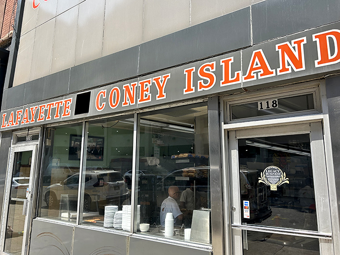 The iconic storefront rivalry on full display – Lafayette's understated gray exterior stands in stark contrast to American's patriotic flair, like two siblings with completely different personalities.