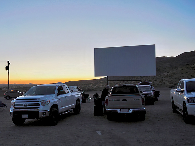 Trucks lined up at sunset, their silhouettes framed against the massive screen—this is how movies were meant to be experienced, under an open desert sky.