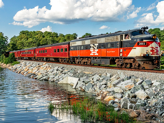 The iconic red and orange locomotive glides alongside Cape Cod's shimmering waters, proving that sometimes the journey truly is the destination.