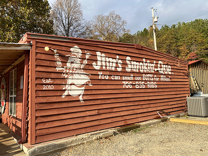 The rustic charm of Jim's Smokin' Que's exterior promises authentic barbecue with its weathered wood and playful pig mascot declaring "You can smell our butts for miles!"