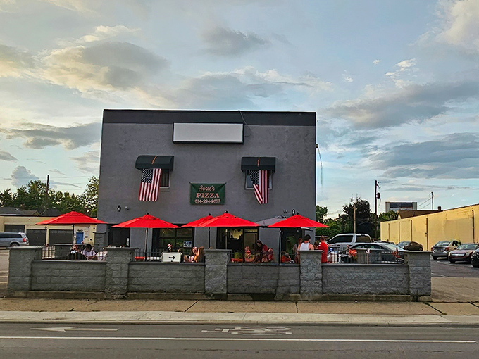 The unassuming gray exterior of Josie's Pizza stands like a humble guardian of flavor, with cheerful red umbrellas beckoning pizza pilgrims to enter pizza paradise.