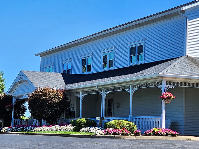 The classic white farmhouse exterior of Amish Door welcomes you with colorful flower beds and a wraparound porch that practically whispers "come sit a spell."