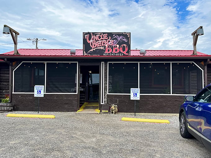 The rustic log cabin with its bright red roof stands like a beacon of barbecue hope in North Lewisburg, with the Uncle Beth&rsquo;s BBQ sign serving as a true bat signal for meat lovers.