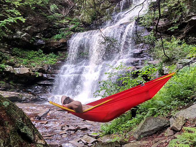 Nature's ultimate relaxation station: a vibrant red hammock perfectly positioned for waterfall viewing. Who needs a sound machine when you've got the real thing?