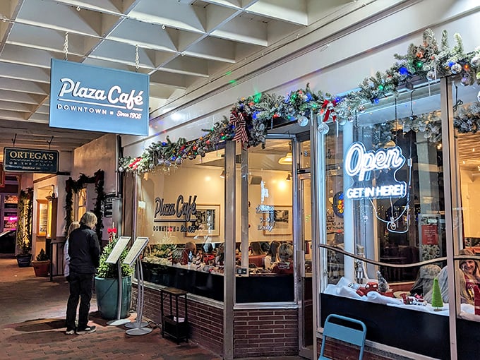 The iconic blue Plaza Café sign beckons like an old friend, promising comfort food with a Southwestern twist beneath festive holiday decorations.