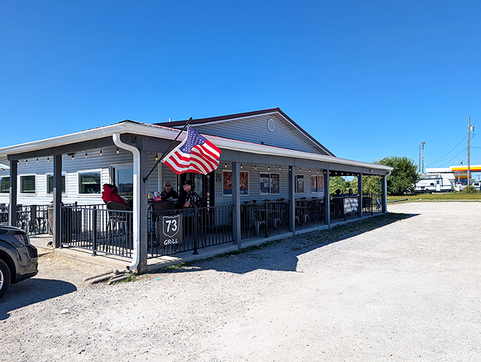 The American flag waves proudly outside 73 Grill, a humble roadside haven where culinary treasures await behind that unassuming beige exterior.