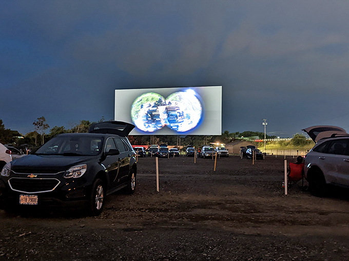 Movie magic comes alive as twilight falls, with cars nestled in neat rows facing the glowing screen. Cinema's most democratic experience awaits.