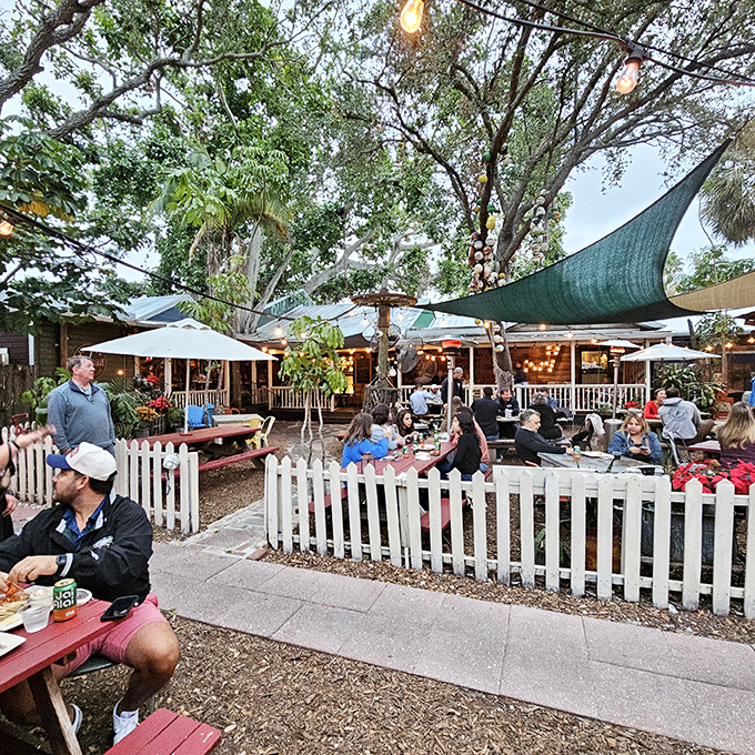 Where white picket fences meet Florida charm. This isn't just outdoor dining; it's a community gathering under the shade sails.