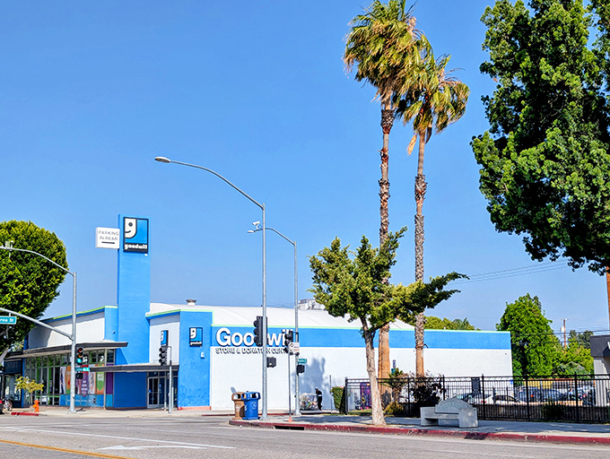 The iconic blue exterior of Goodwill Burbank stands like a beacon of bargain possibilities under the California sun, palm trees included.