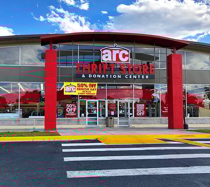 The red-trimmed facade of arc Thrift Store stands like a treasure chest waiting to be opened, promising adventures in secondhand splendor.