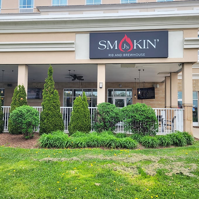 The welcoming facade of Smokin' J's beckons with manicured greenery and a promise of smoky delights within. That sign isn't just decoration—it's a beacon for hungry souls.