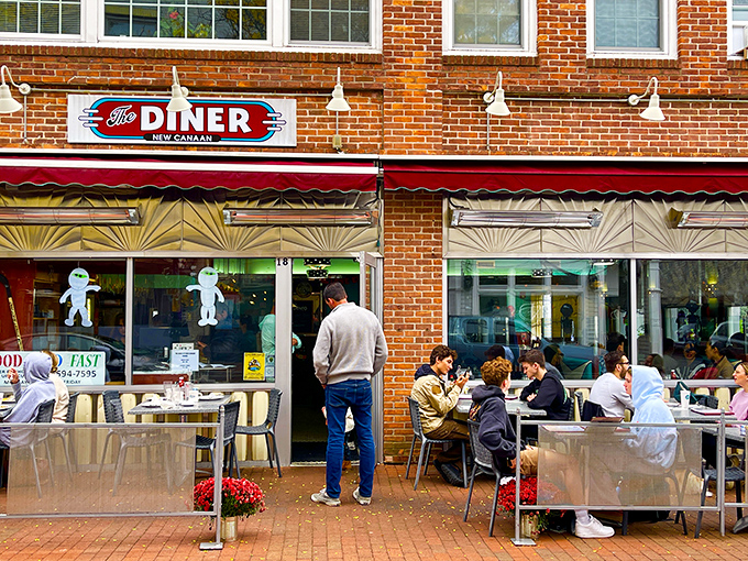 The classic red neon sign beckons like an old friend. Brick facade, red awning, and outdoor seating create the perfect small-town Connecticut charm.