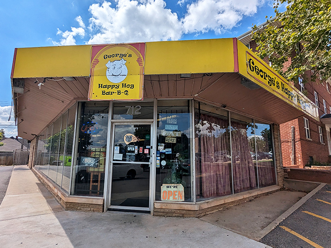 That bright yellow awning with the smiling cartoon pig is a beacon of barbecue hope—no frills, just the promise of smoky goodness waiting inside.