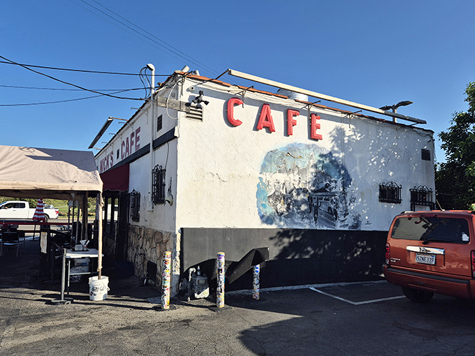 The unassuming white exterior of Nick's Cafe stands like a time capsule in industrial Los Angeles, its bold red lettering promising simple pleasures within.