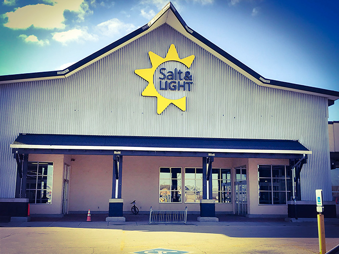 The distinctive yellow sun logo of Salt & Light Thrift shines like a beacon of bargain hope against the corrugated metal exterior, promising treasures within.