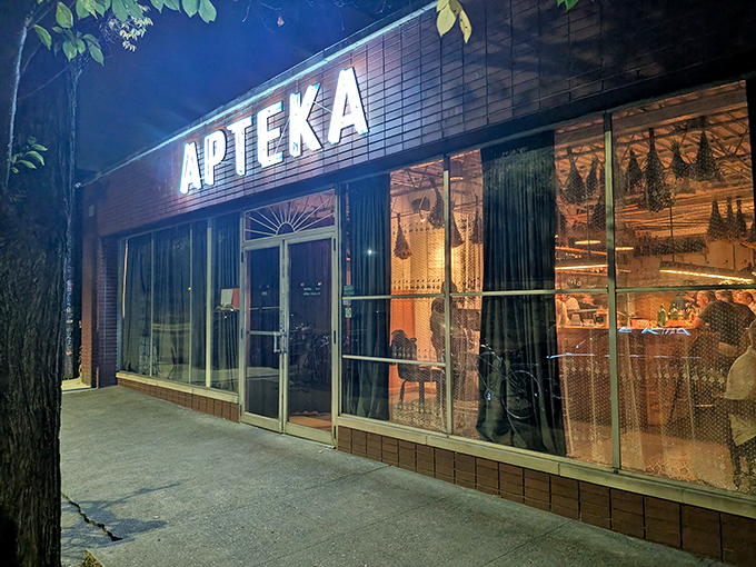 Apteka's illuminated storefront beckons like a warm lighthouse on a Pittsburgh evening, promising plant-based Polish treasures within those brick walls.