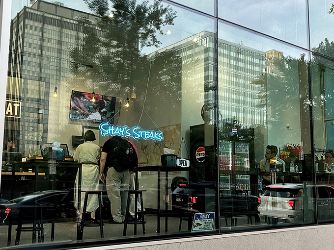 Through these windows lies sandwich salvation. The city's skyscrapers reflect in the glass, as if they too are eyeing what's cooking inside.