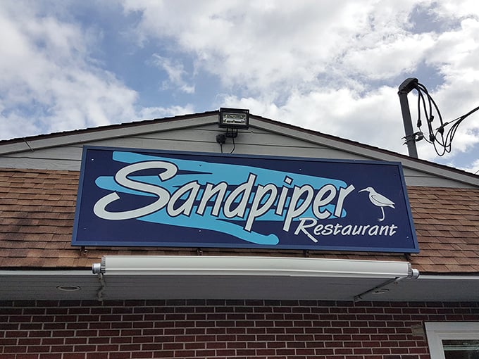 The blue Sandpiper sign beckons like a lighthouse for hungry travelers. Seafood, steaks, and hot dogs await beneath those weathered shingles.