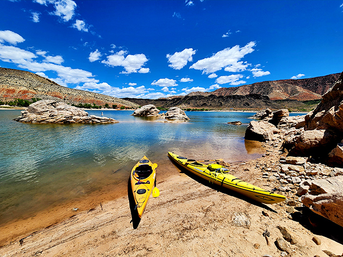 Two bright yellow kayaks rest on the shoreline like eager puppies waiting for adventure, while the turquoise waters of Gunlock Reservoir stretch toward rust-colored mountains.