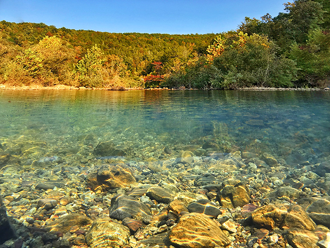 Crystal-clear water meeting ancient rock under autumn's golden canopy &ndash; nature's own infinity pool without the resort fees.