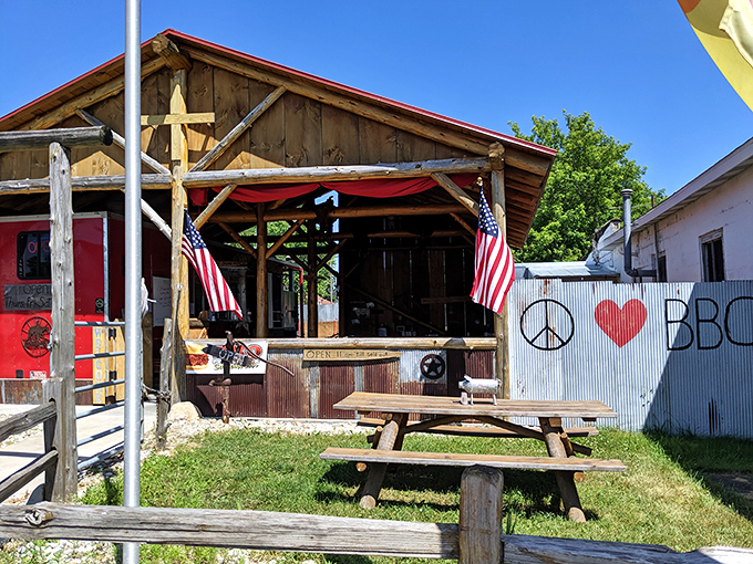 Rustic charm personified! American flags flutter beside a wooden shack that promises smoky delights and picnic table conversations under Michigan's blue skies.