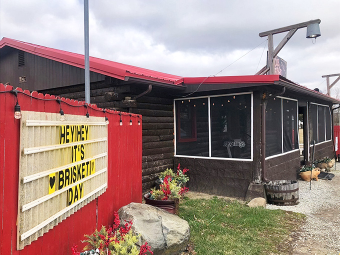 The rustic log cabin with its bright red roof stands like a beacon of barbecue hope in North Lewisburg. That "Hey Hey It's Brisket Day" sign is basically a bat signal for meat lovers.