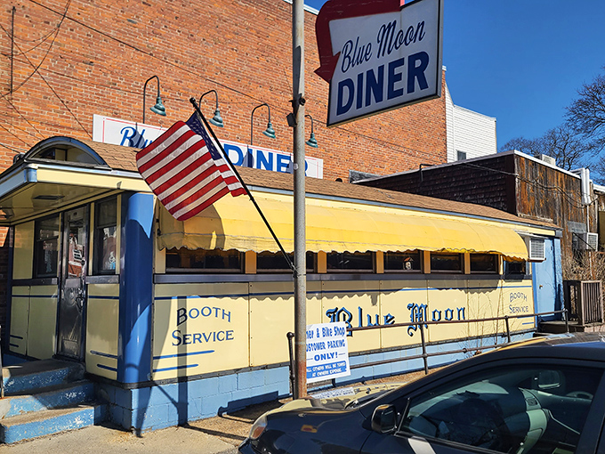 The classic yellow exterior of Blue Moon Diner stands like a time capsule on Gardner's Main Street, complete with vintage signage and an American flag that says "real diner ahead."