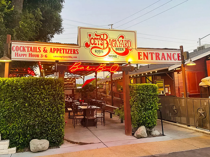 "Joey's Backyard" entrance beckons with neon glow and strategically placed greenery &ndash; your portal to barbecue nirvana in Chino.