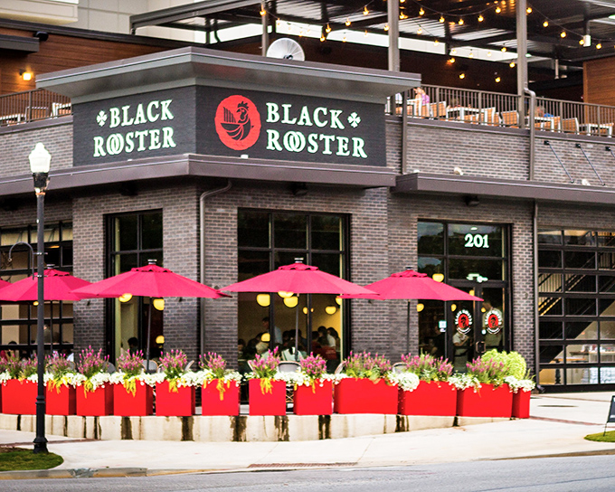 The brick fortress of flavor beckons with its vibrant red planters and cheerful umbrellas&mdash;Black Rooster's exterior promises culinary adventures within.