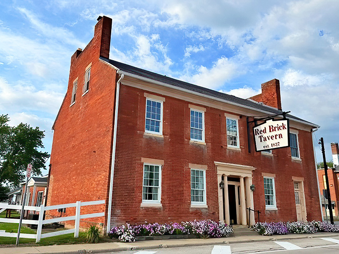 The Red Brick Tavern stands proudly along Route 40, its historic façade practically whispering tales from the 1800s while colorful flower beds add a welcoming touch.