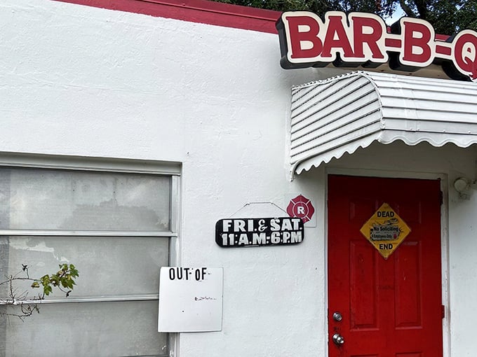 The humble white building with its red smoker attachment stands like a barbecue beacon under Florida oaks, promising smoky treasures within.