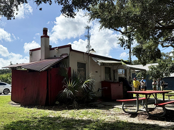 The humble white building with its red smoker attachment stands like a barbecue beacon under Florida oaks, promising smoky treasures within.