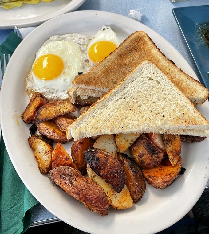 Two sunny-side-up eggs with that perfect runny yolk potential, ready to transform ordinary toast into extraordinary breakfast magic. Those home fries deserve their own fan club.