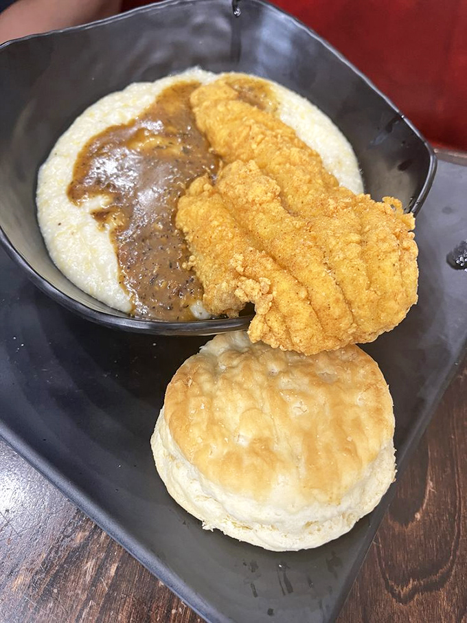 Crispy catfish lounging on creamy grits like it's on vacation, with a biscuit chaperone keeping watch nearby.