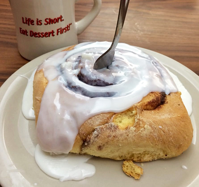 A cinnamon roll drowning in icing with a coffee mug that speaks truth: "Life is Short. Eat Dessert First." Words to live by, friends.