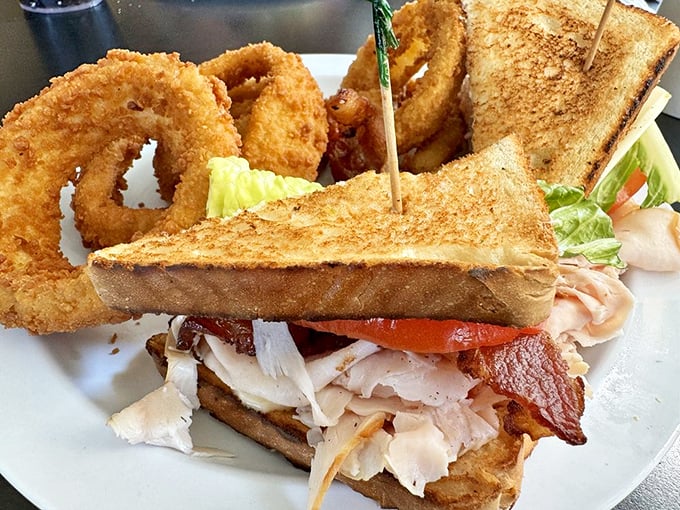 A club sandwich that stands taller than your retirement dreams, flanked by onion rings with the perfect crunch-to-tenderness ratio.
