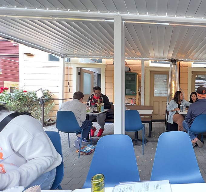 The outdoor patio offers a garden-adjacent dining experience. Blue chairs pop against the greenery&mdash;California al fresco at its finest.