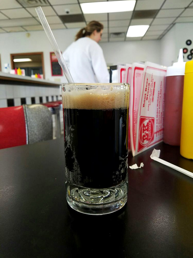 The root beer arrives in a frosted mug, dark and mysterious, crowned with a foamy head that whispers sweet promises of refreshment.