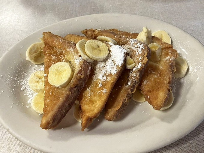 French toast that looks like it's auditioning for a breakfast calendar spread—golden, dusted with powdered sugar, and adorned with banana slices for that touch of fancy.